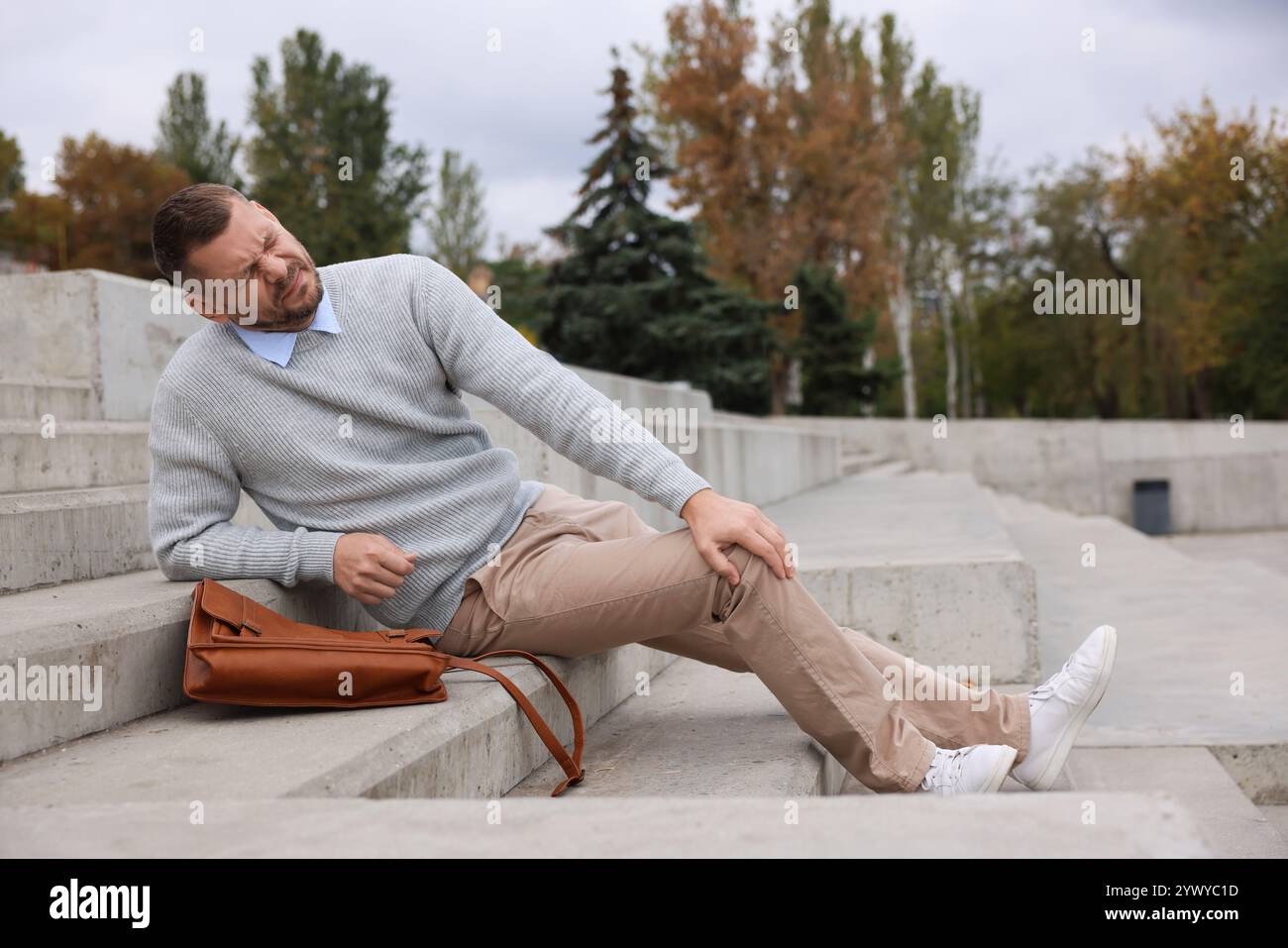 Man with injured leg on stairs outdoors after fall. Dangerous accident ...