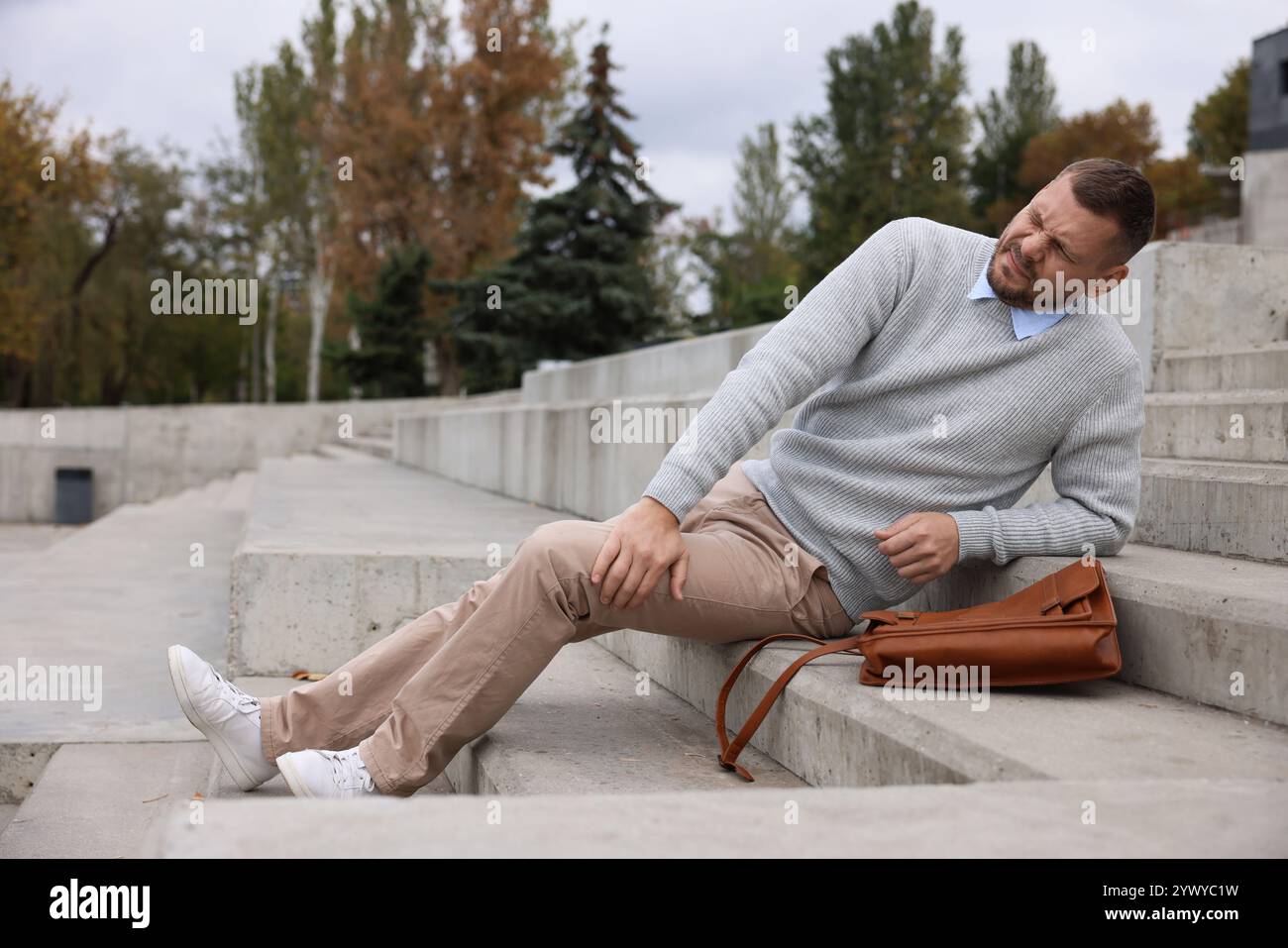 Man with injured leg on stairs outdoors after fall. Dangerous accident ...