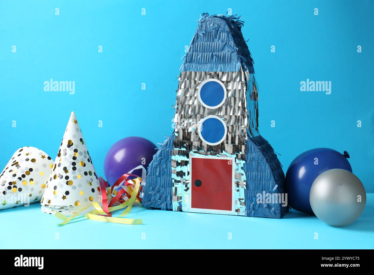 Beautiful pinata in shape of rocket, party cones and balloons on blue ...