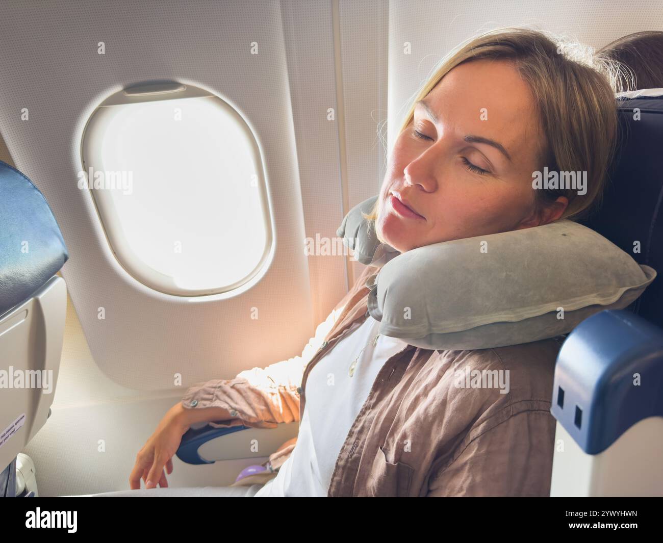 Rest on plane. Young woman napping sitting by porthole in business jet ...
