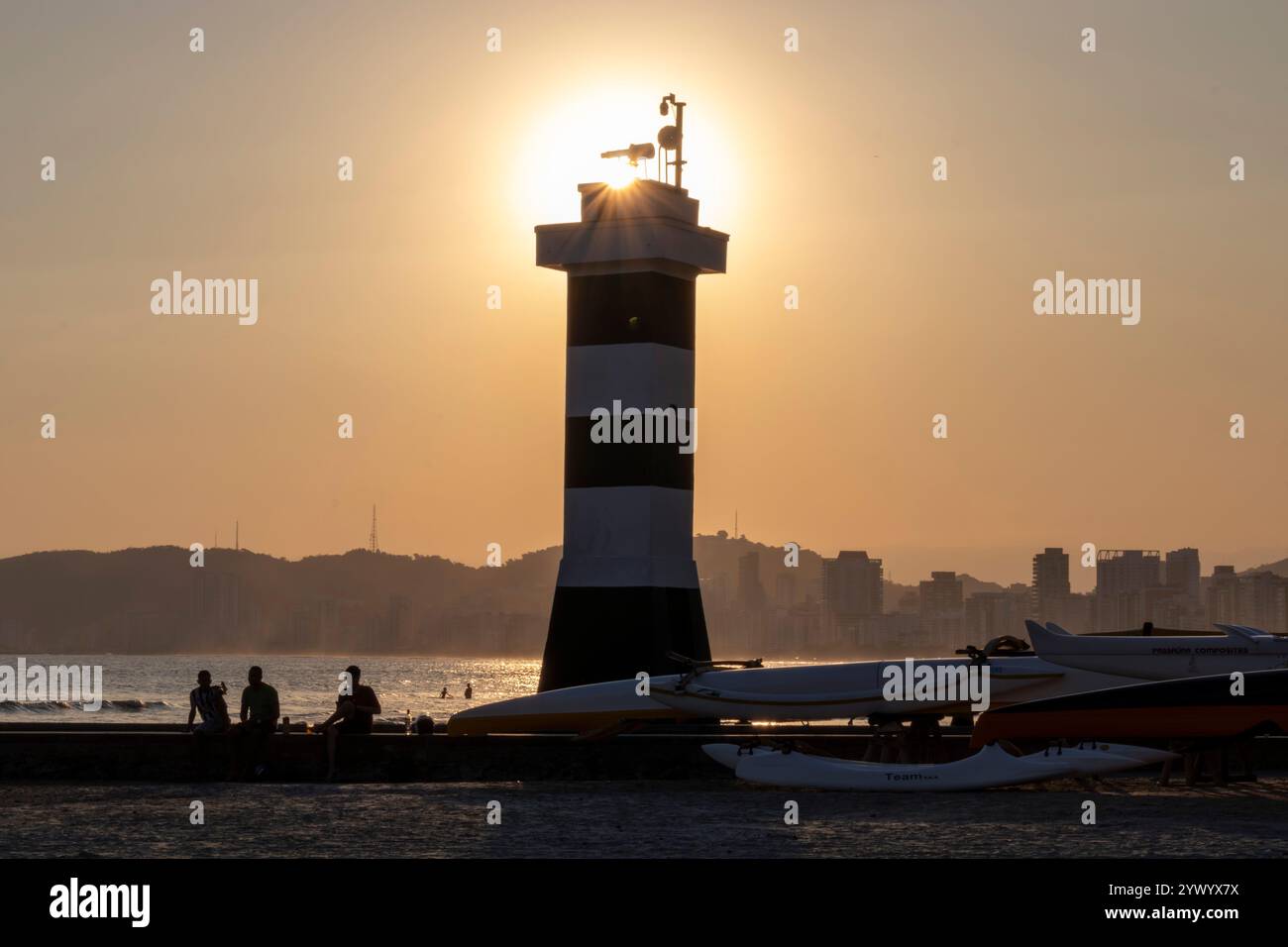 A black and white striped lighthouse with the sun setting directly ...
