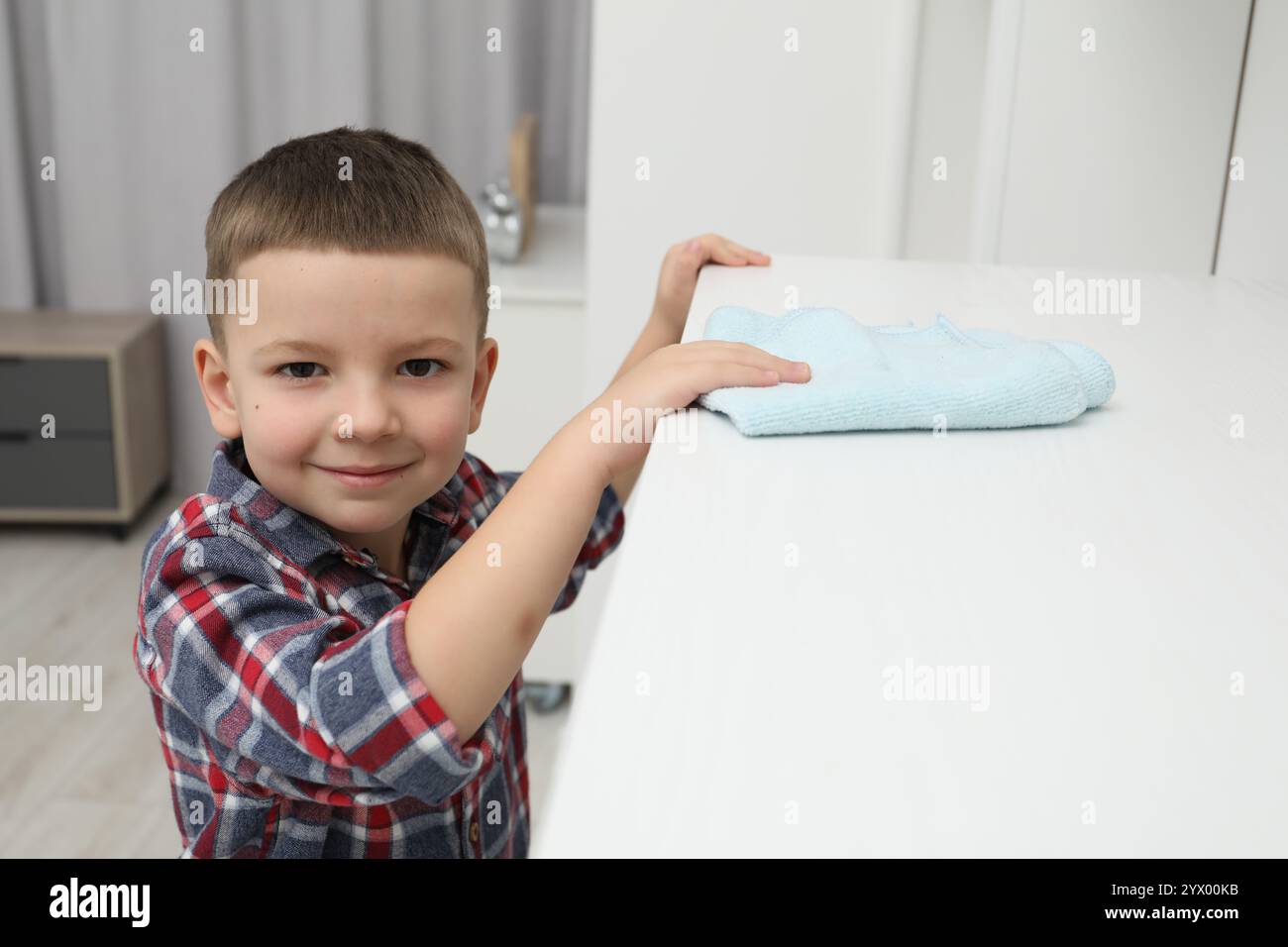 Little helper. Cute boy wiping dust from chest of drawers at home Stock ...