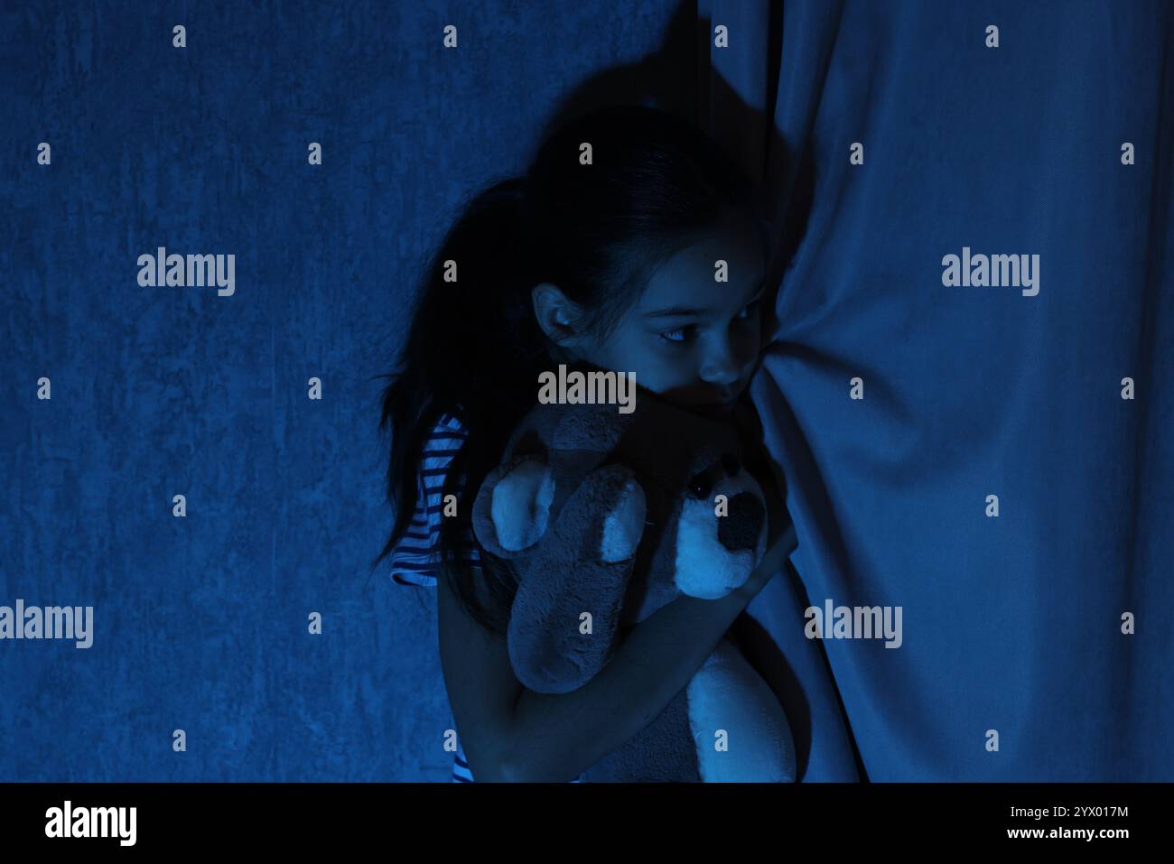 Scared girl hiding with teddy bear behind curtain at night. Space for ...