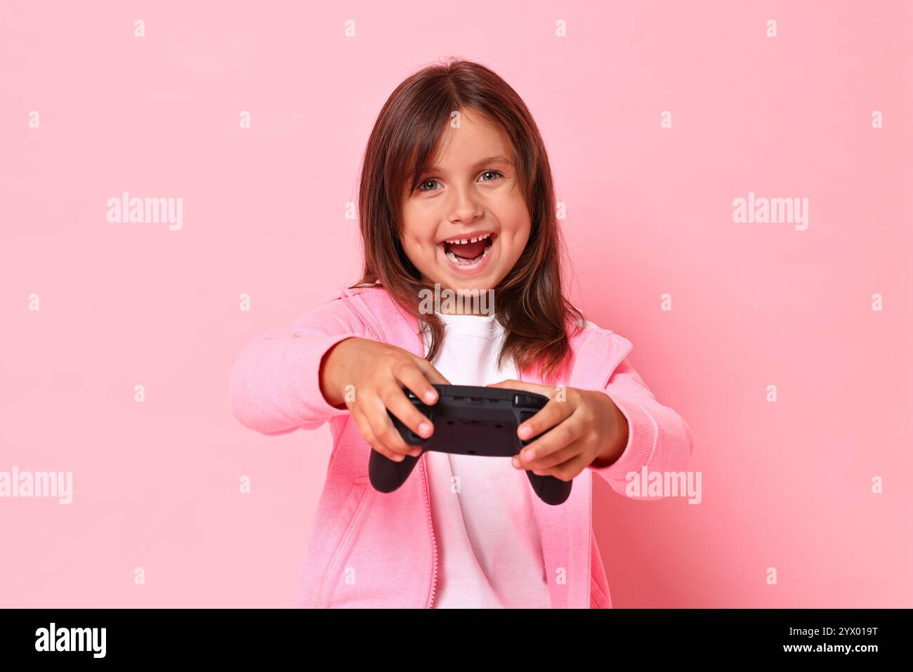 Happy little girl playing video game with controller on pink background ...