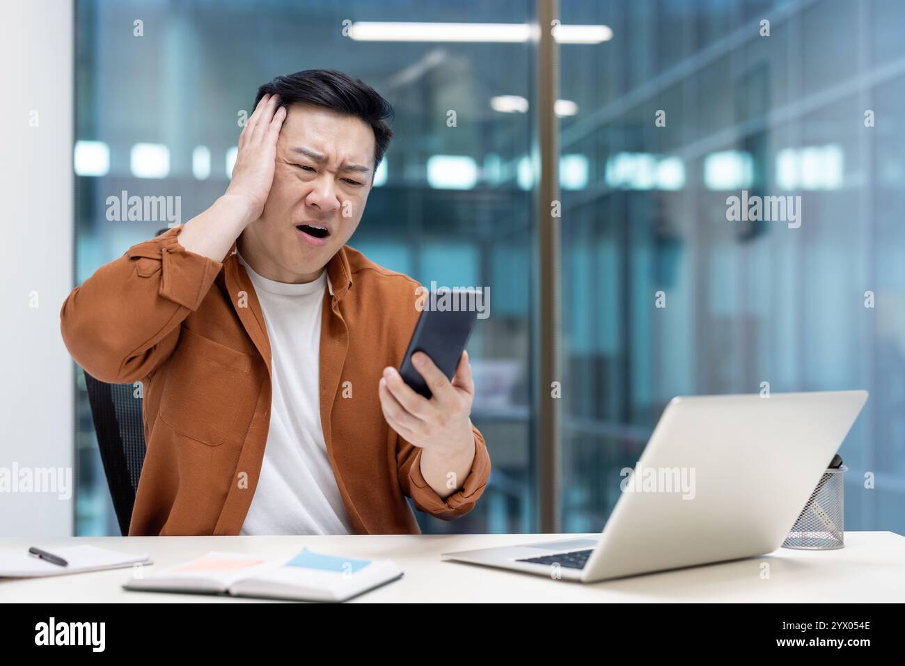 Asian man experiencing frustration looking at his smartphone in a ...