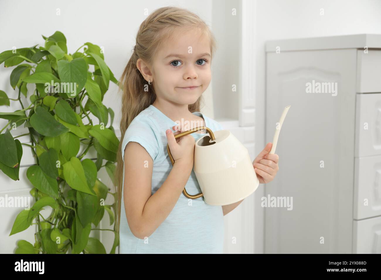 Little helper. Cute girl with watering can at home Stock Photo - Alamy