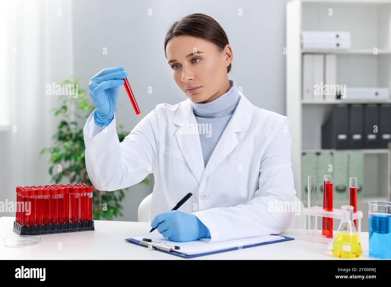 Laboratory testing. Doctor with blood sample taking notes at table ...