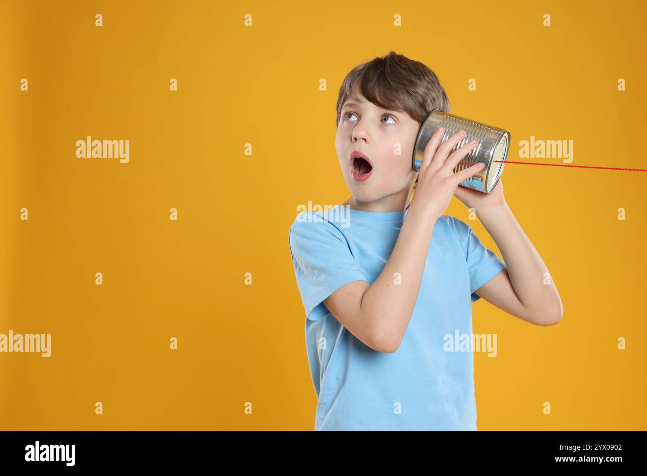 Surprised boy using tin can telephone on orange background. Space for ...