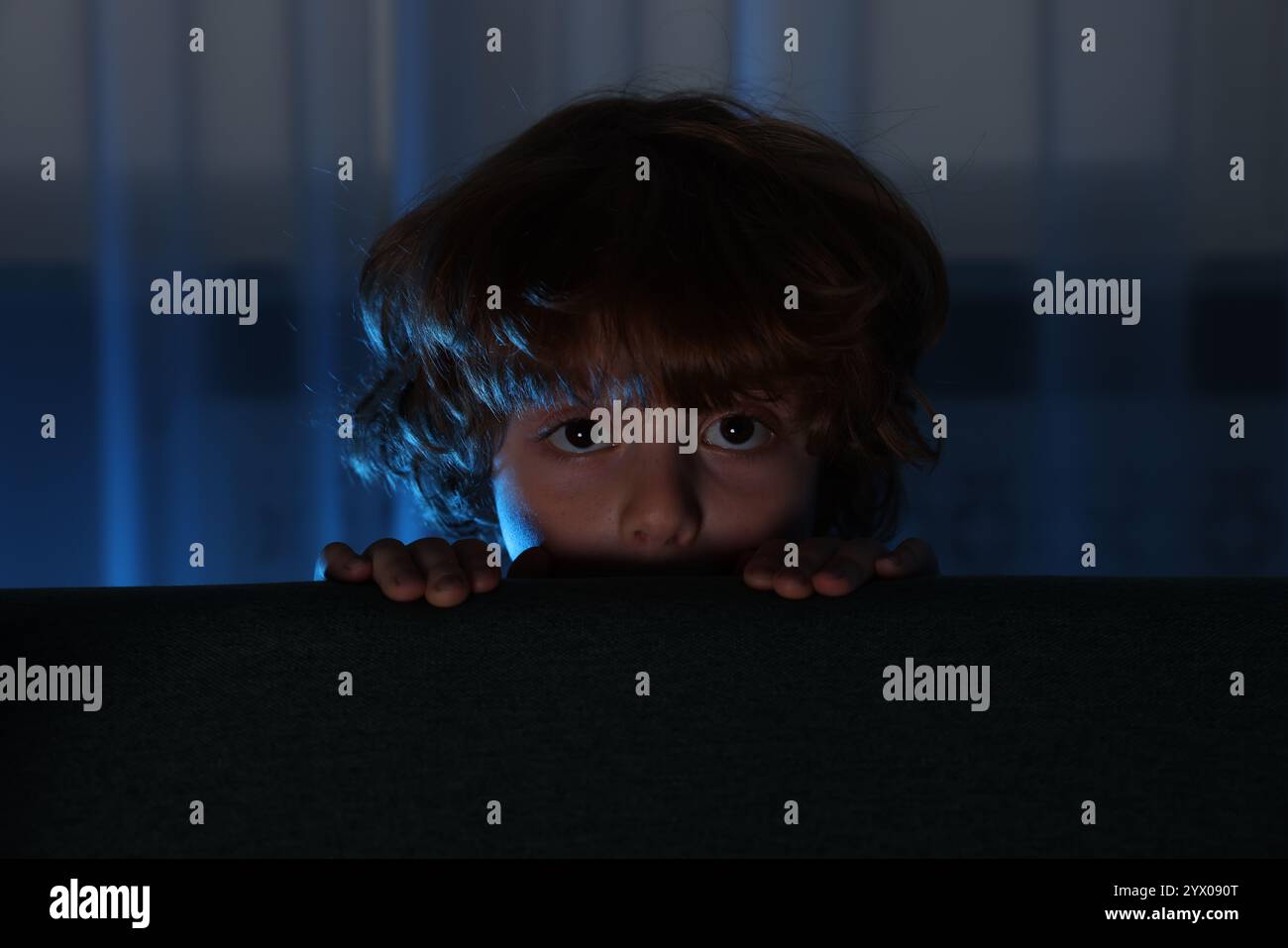 Fearful boy hiding behind sofa at night Stock Photo - Alamy