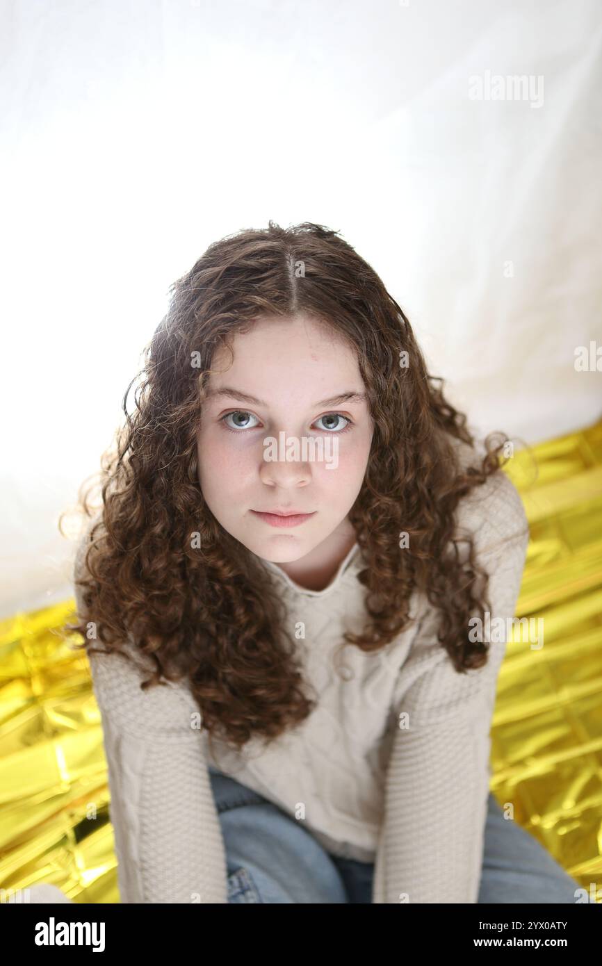 Teenage girl sitting on gold sheet survivial blanket curly hair cream ...