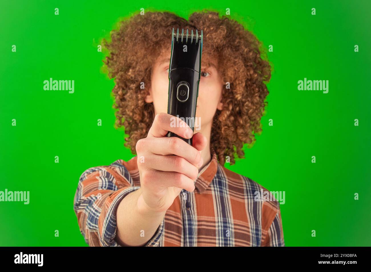 A curly-haired boy in a smart shirt shaves his hair with a steady hand ...