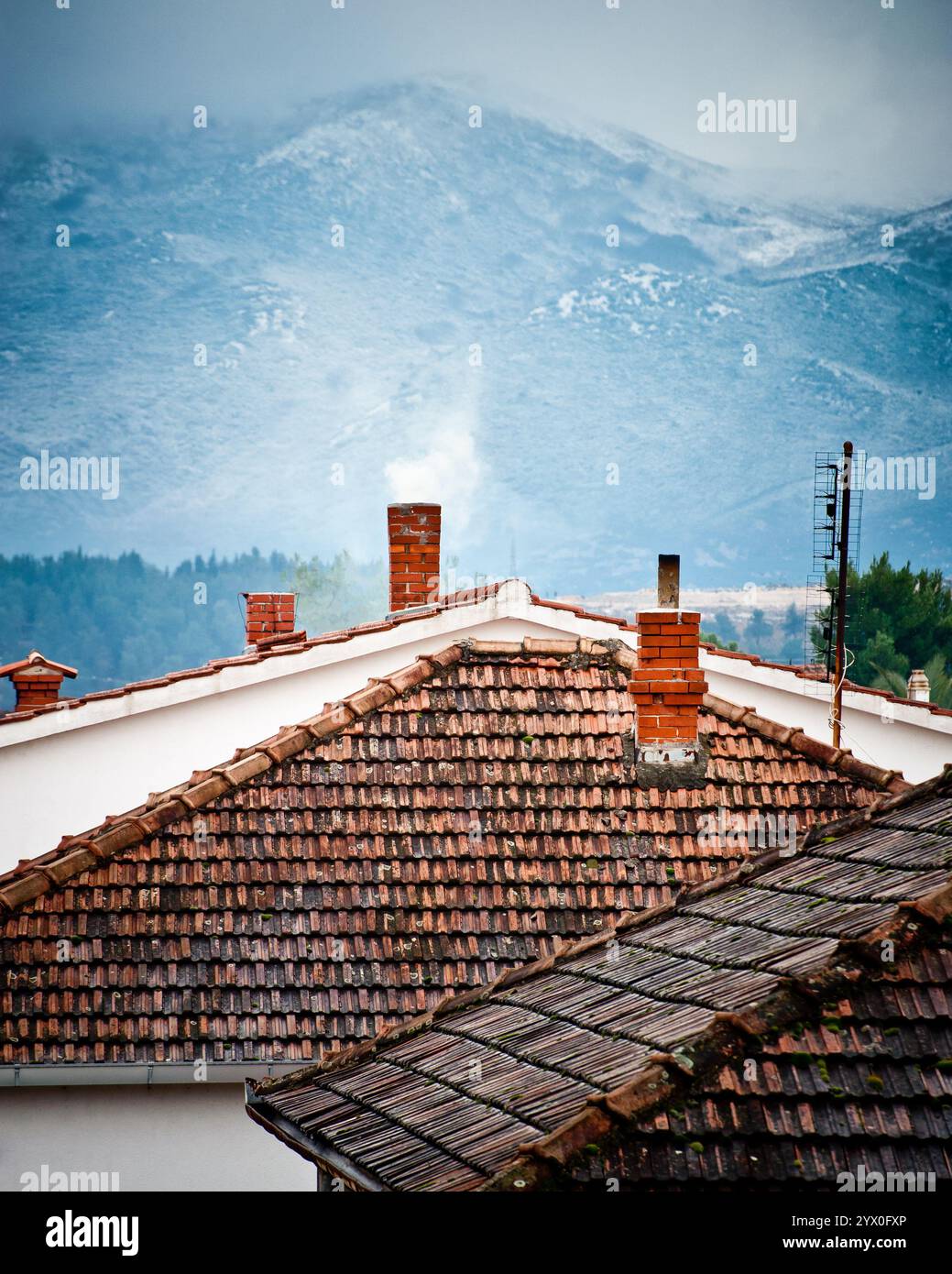 Rooftops with smoking chimneys and snowy hills in the back Stock Photo ...