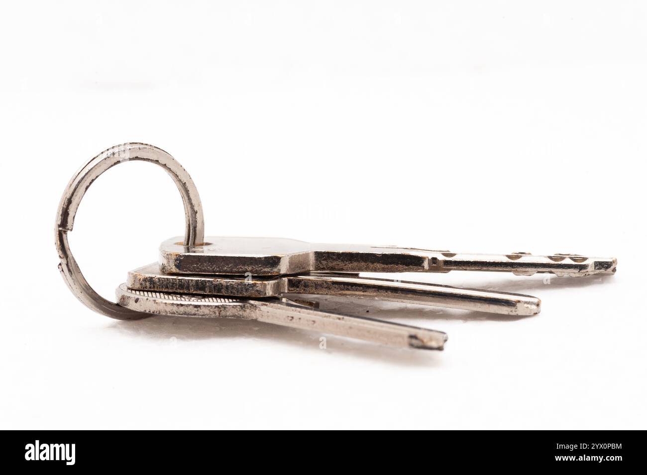 Three keys are hanging from a key chain. The keys are silver and have a ...