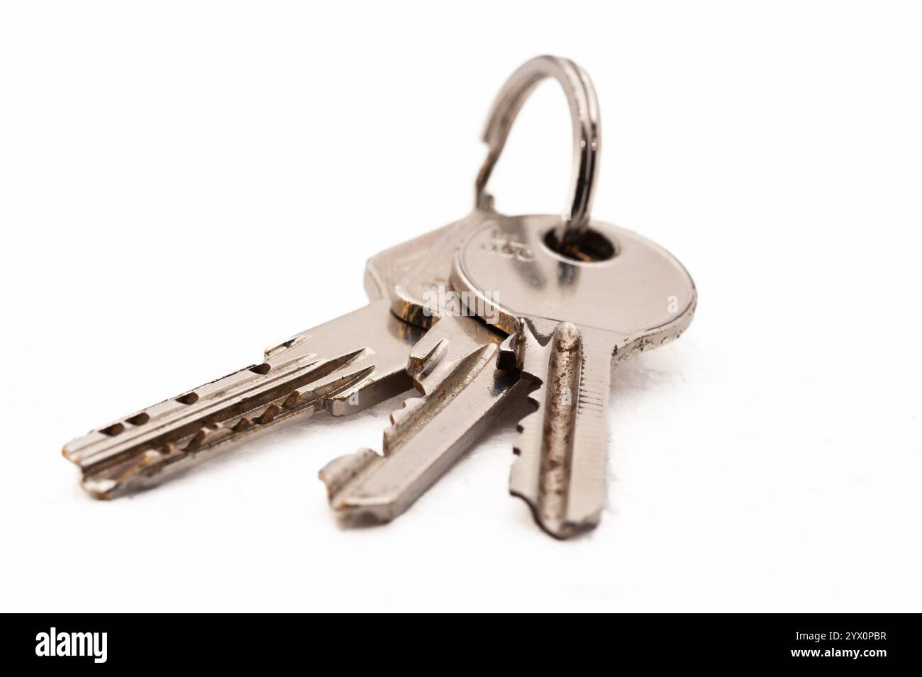 Three keys are hanging from a key chain. The keys are silver and have a ...