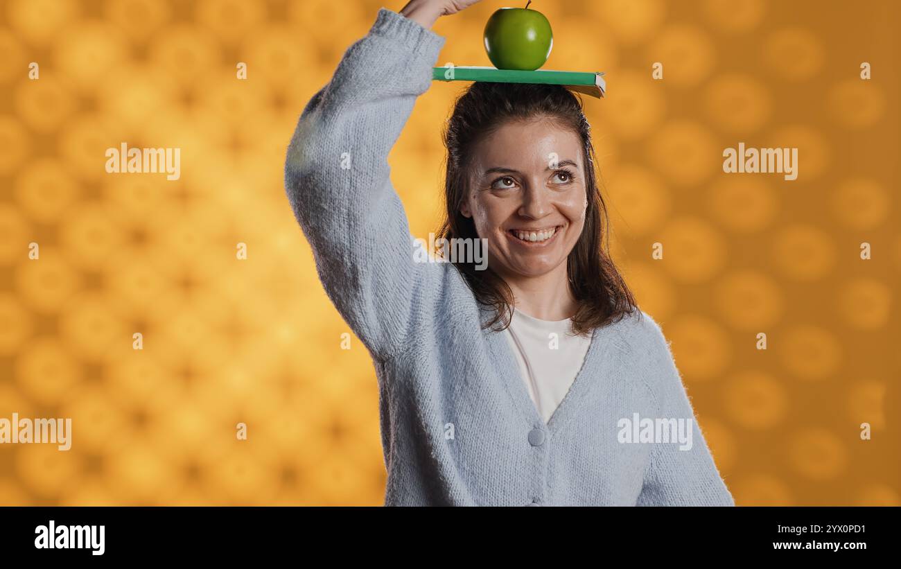 Woman balancing book and apple on head, acting zany, portraying living ...