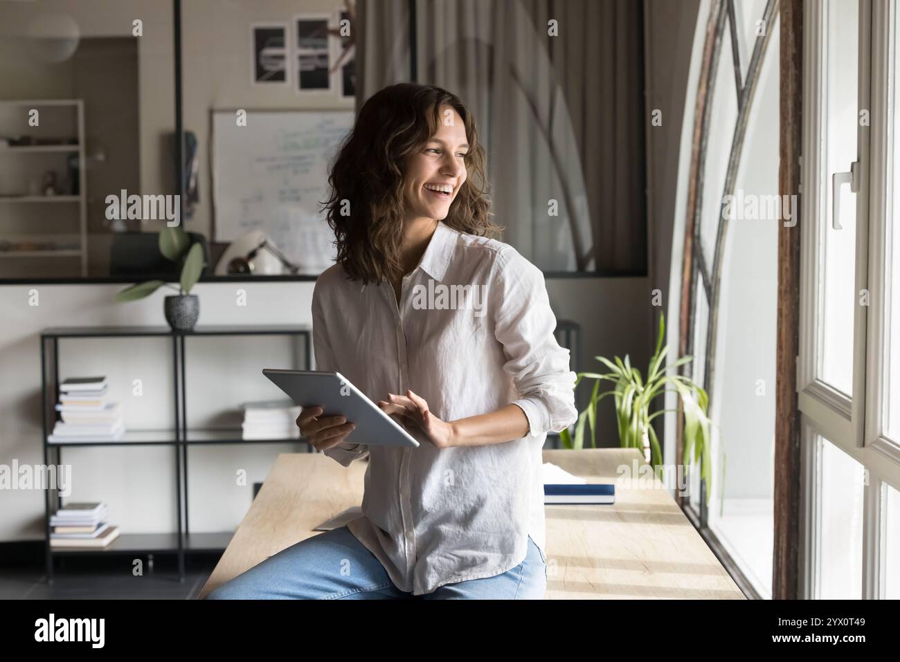 Pretty woman holding tablet, looking out window with smile Stock Photo ...