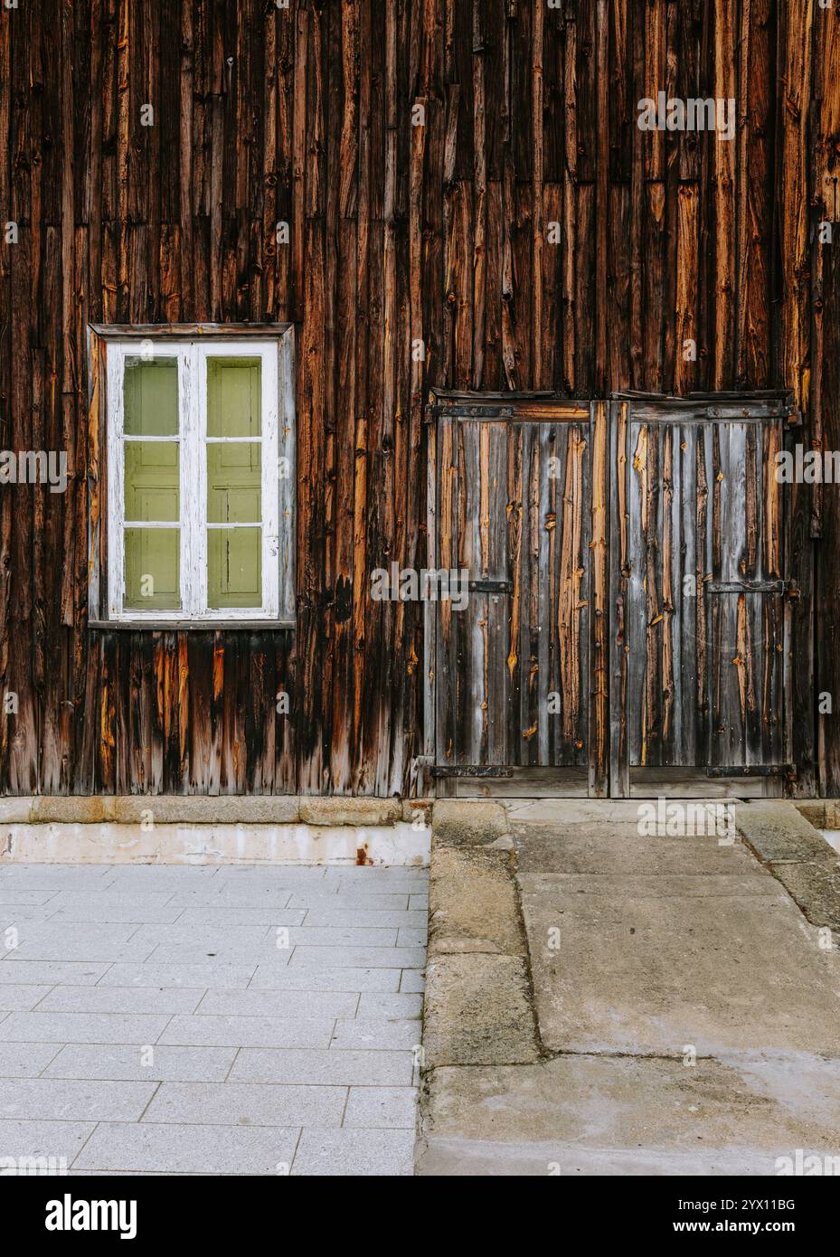Weathered wooden facade featuring a closed double door and a window with faded paint, showcasing ...