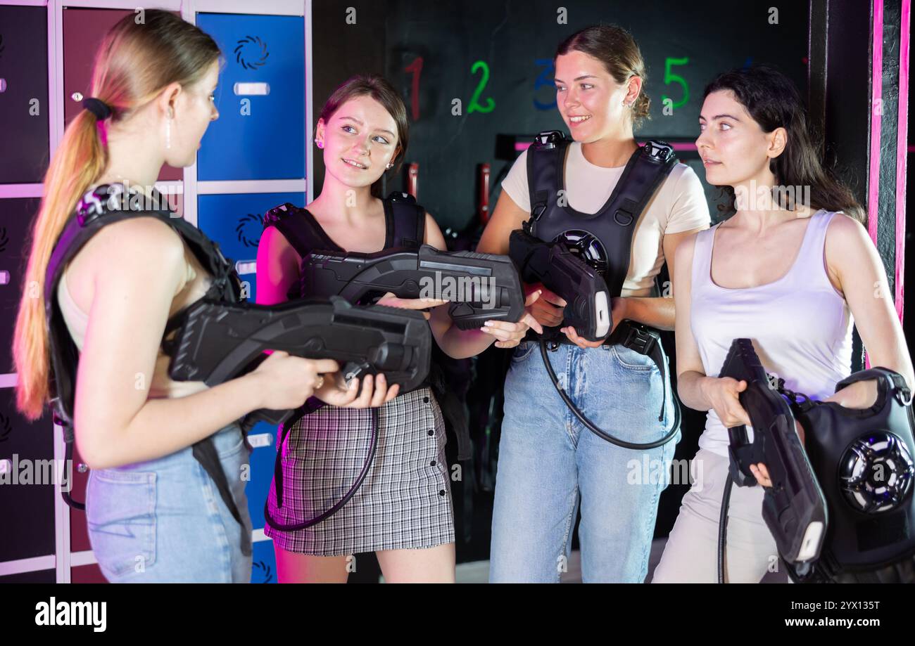 Group of girls in laser tag vests with rifles in their hands are ...