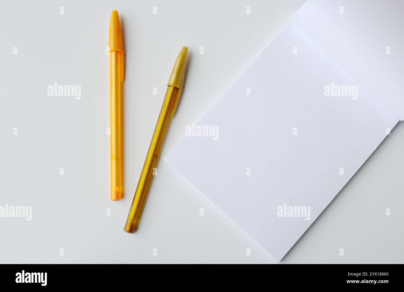 Two golden ballpoint pens on top of a blank paper notepad page ...