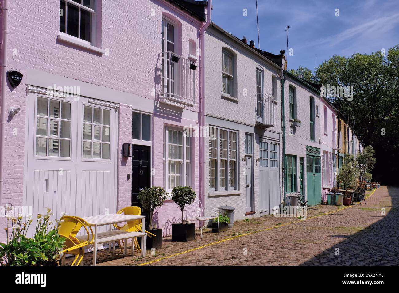 Pastel colour terrace cottages, cobblestones, flowers and tree in ...