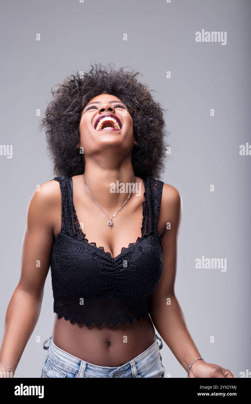Cheerful young black woman laughing joyfully with her head tilted back and mouth wide open ...
