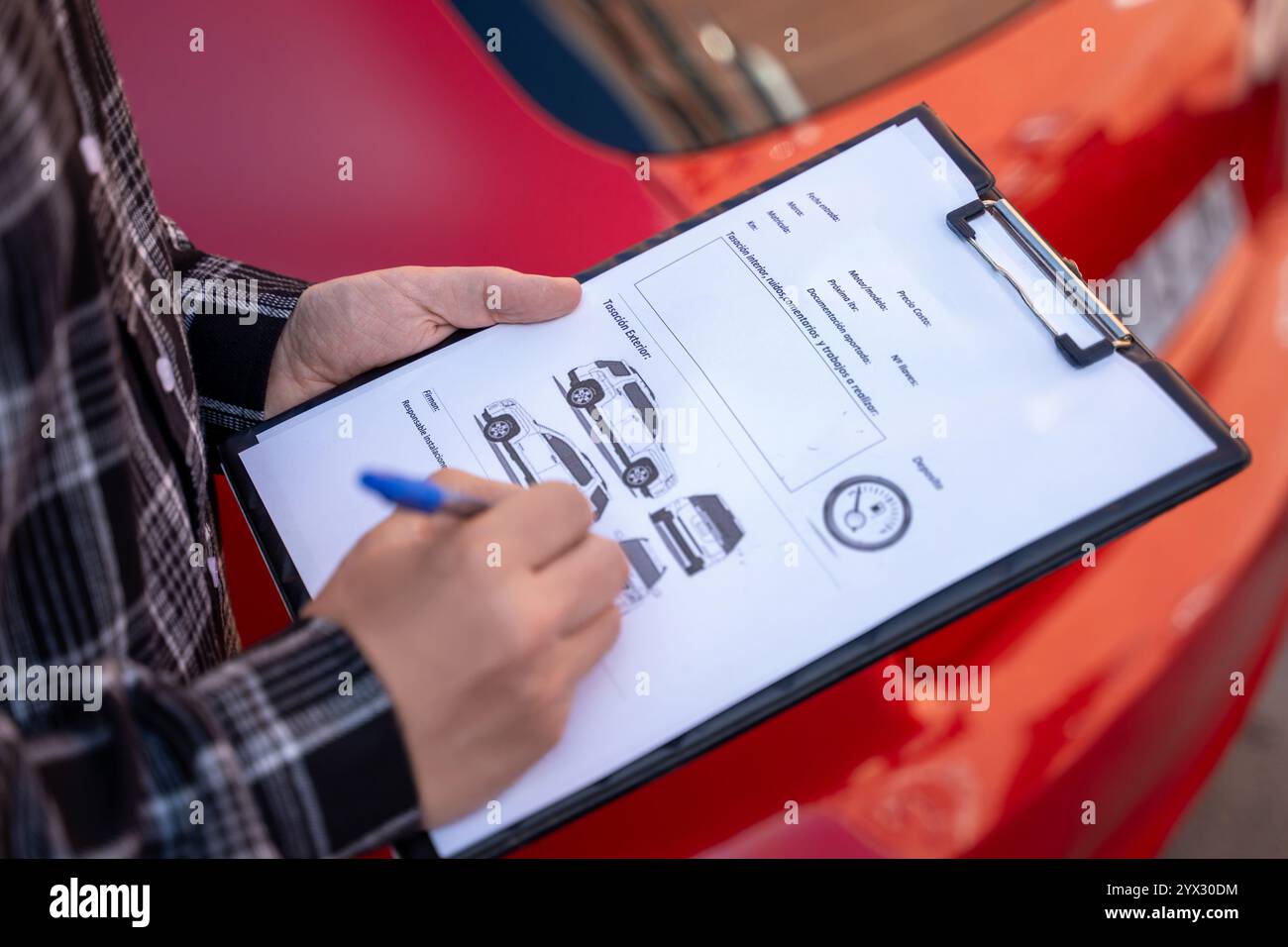 Insurance agent writing notes on clipboard, assessing damage on red car ...