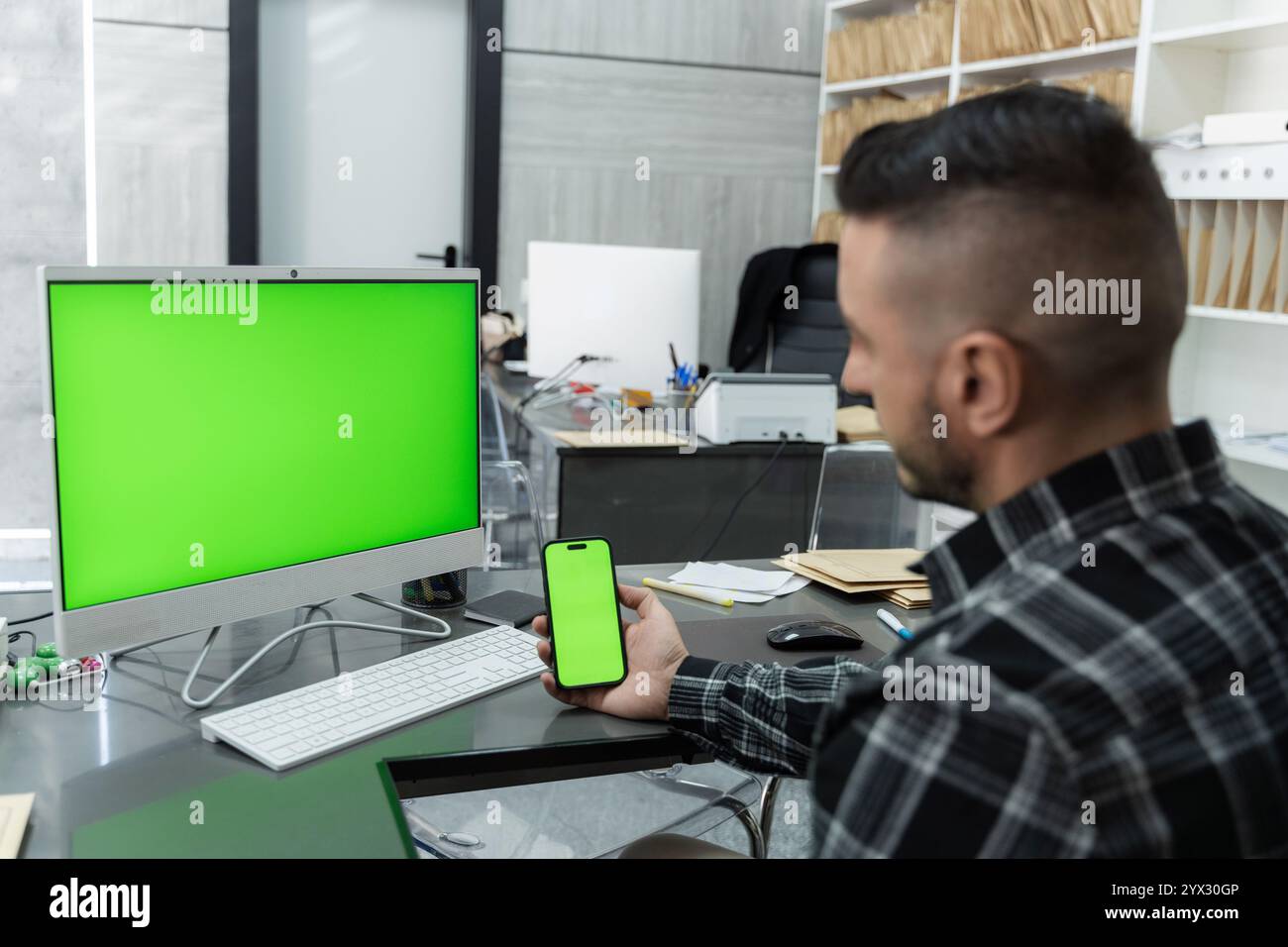 Businessman sitting at desk comparing green screen on computer monitor ...