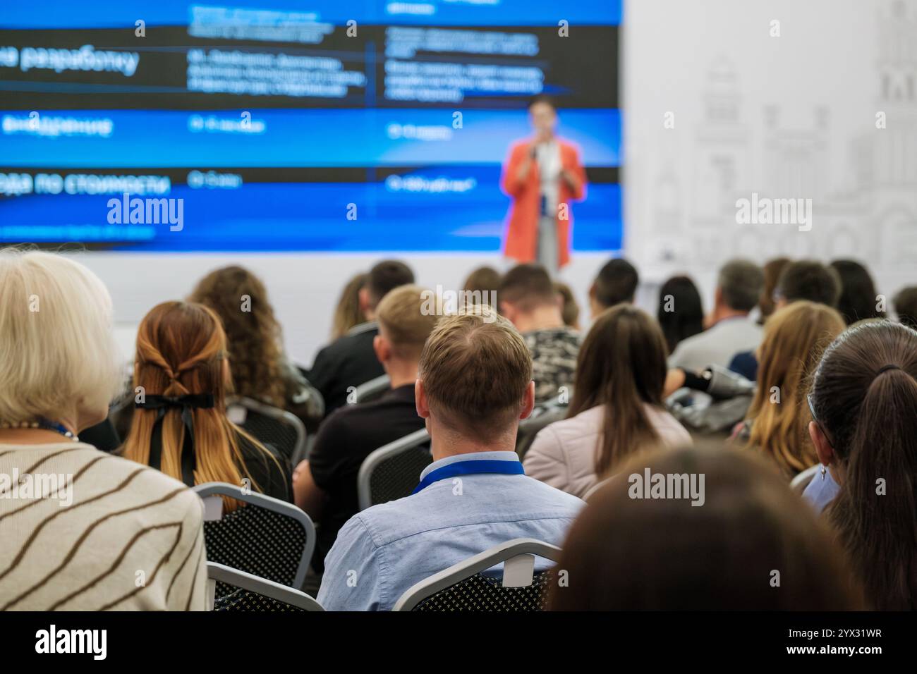 Conference attendees sitting in chairs observing a business speaker ...