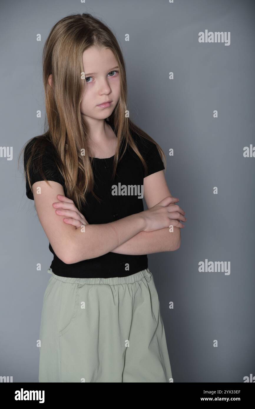 Young girl stands with arms crossed, her solemn face evoking thought. A ...