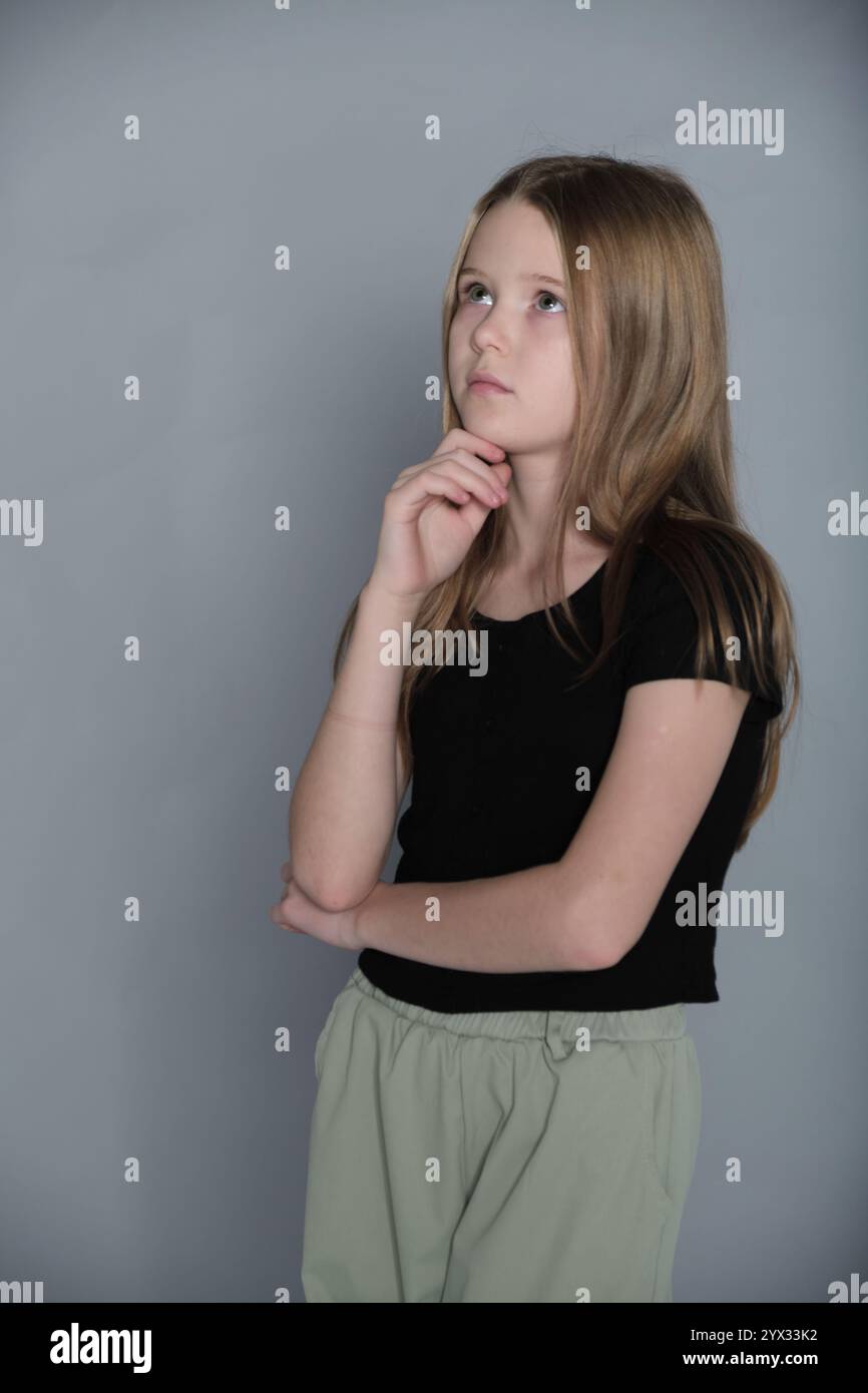 Pensive child with a gentle touch to her face, looking afar. Reflects ...