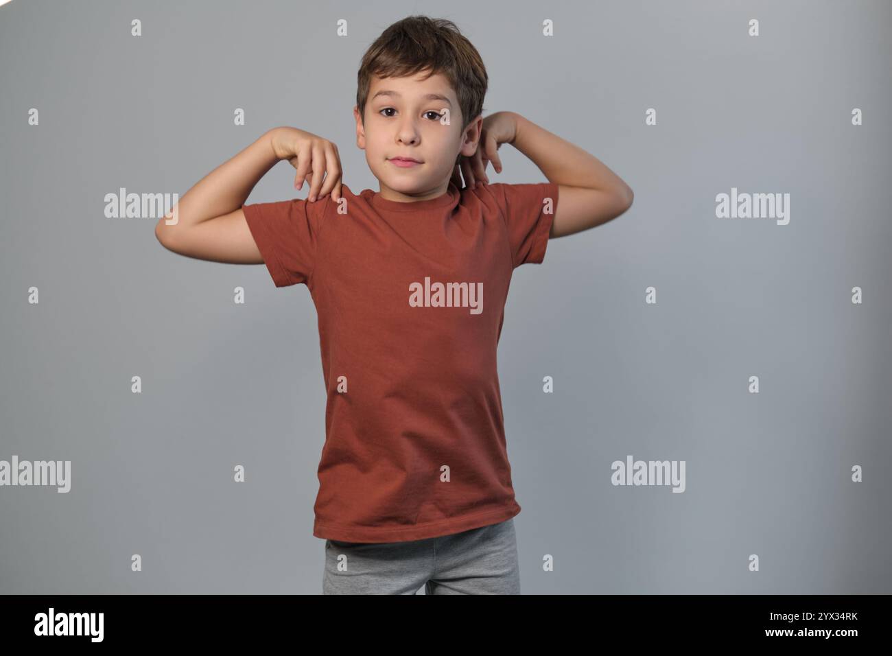 A young boy playfully raises his hands, showing confidence and a ...