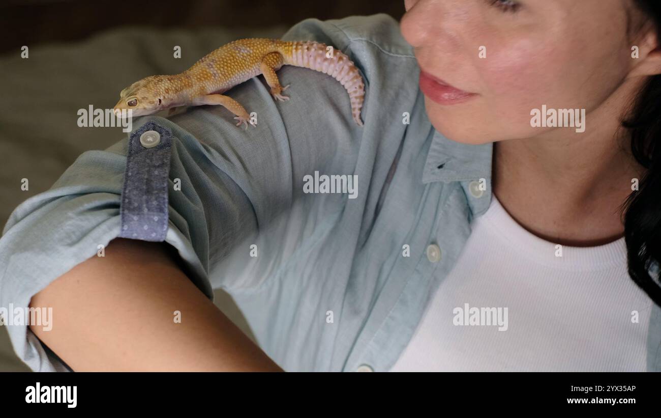 A close-up of a smiling woman interacting with a gecko on her arm. The ...