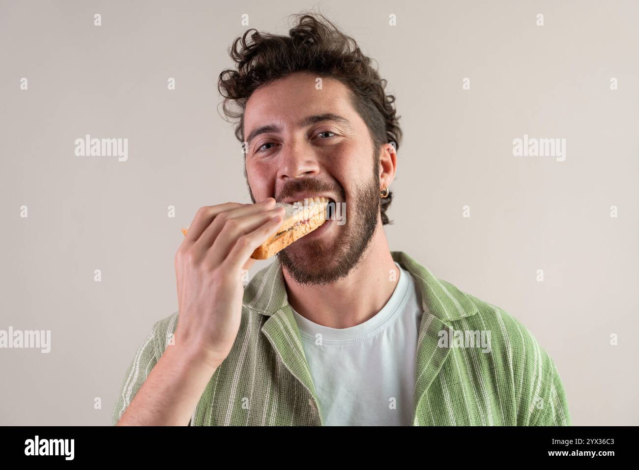 Young man with curly hair eating a sandwich, candid lifestyle ...