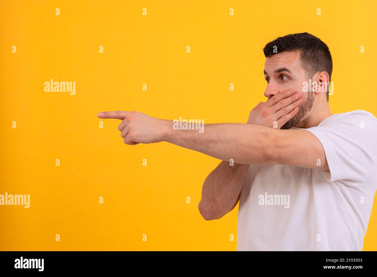 Surprised man pointing and covering his mouth on a yellow background ...