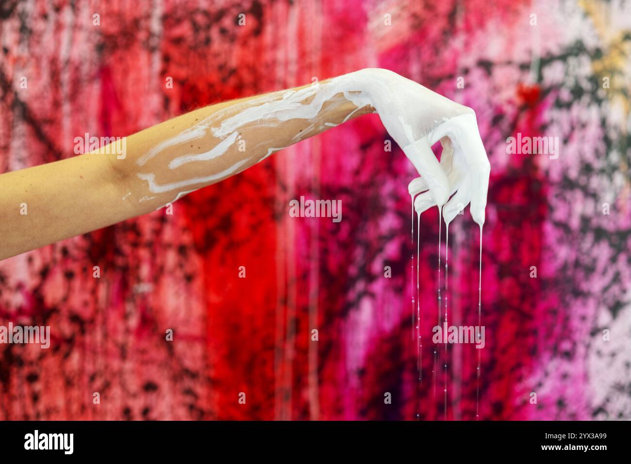 A delicate hand covered in dripping white paint extends gracefully ...