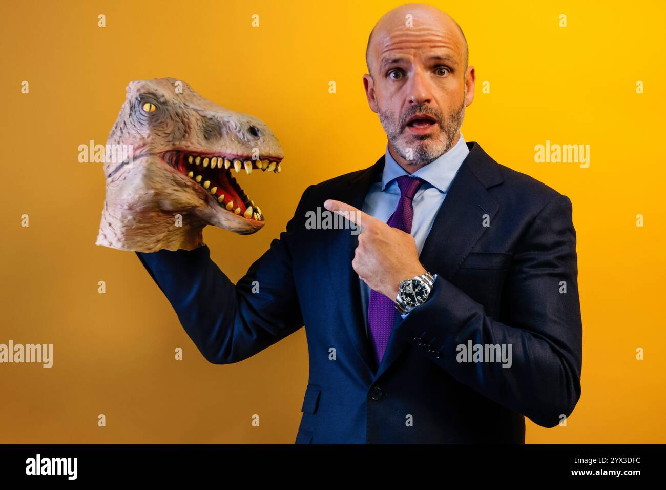 A man in a suit is holding a dinosaur puppet. He is pointing at the ...