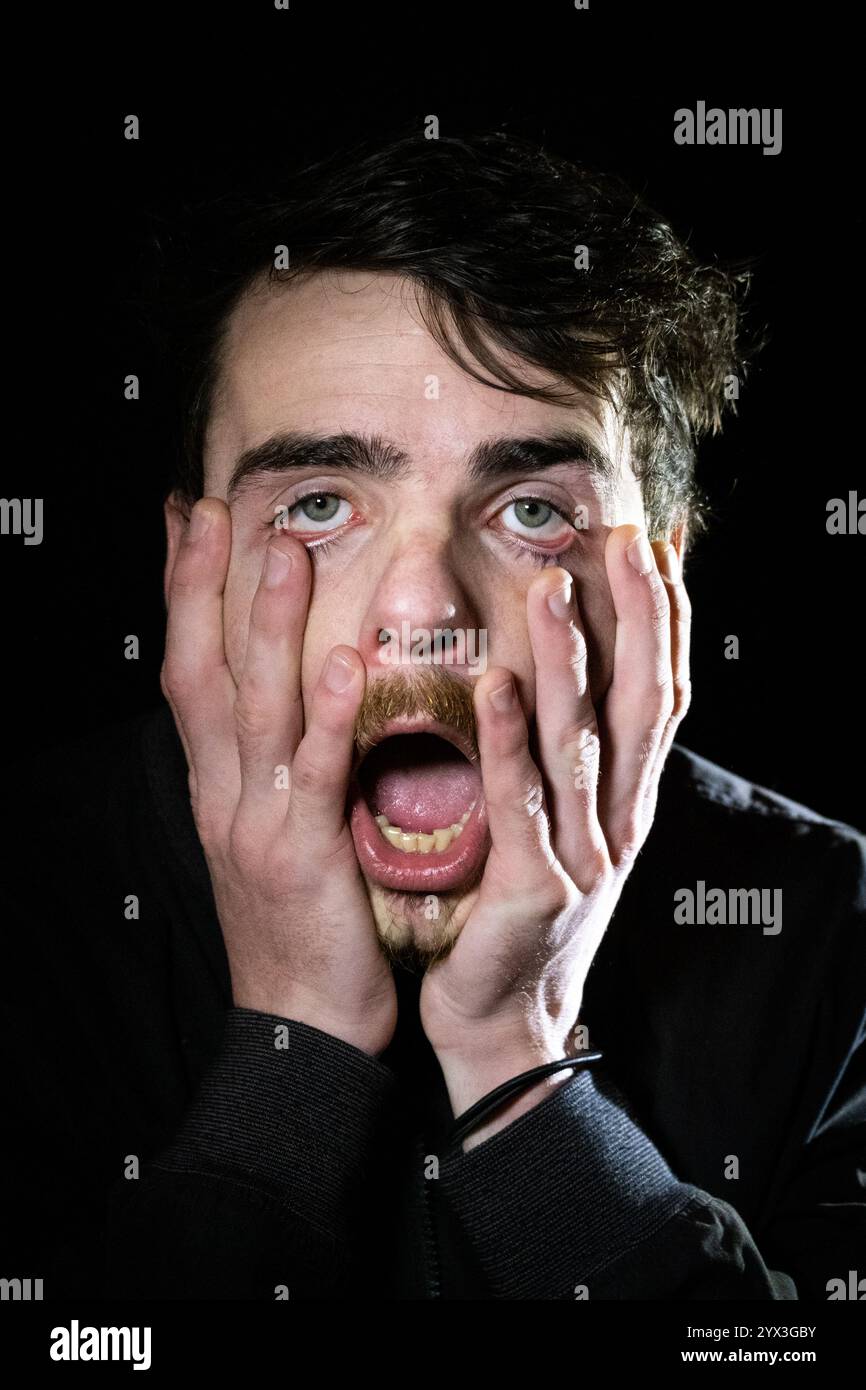 Studio portrait of a young ma with a strange emotion akin to madness or ...