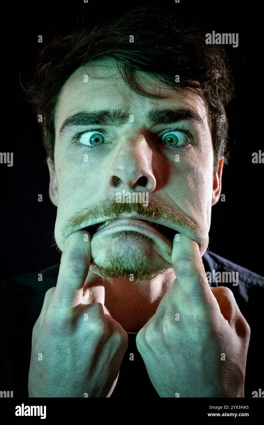 Studio portrait of a young ma with a strange emotion akin to madness or ...