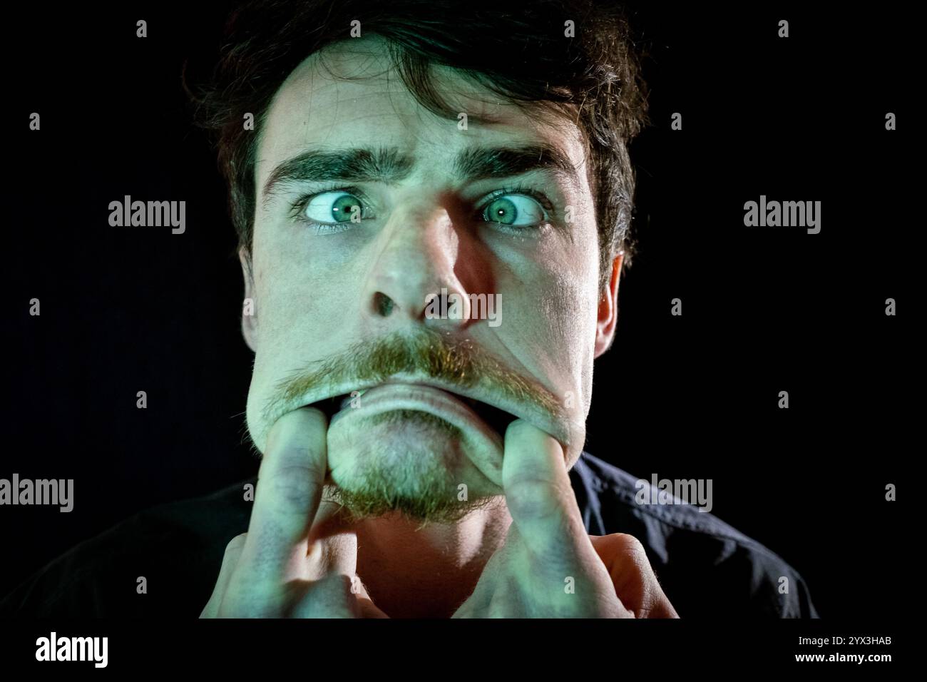 Studio portrait of a young ma with a strange emotion akin to madness or ...