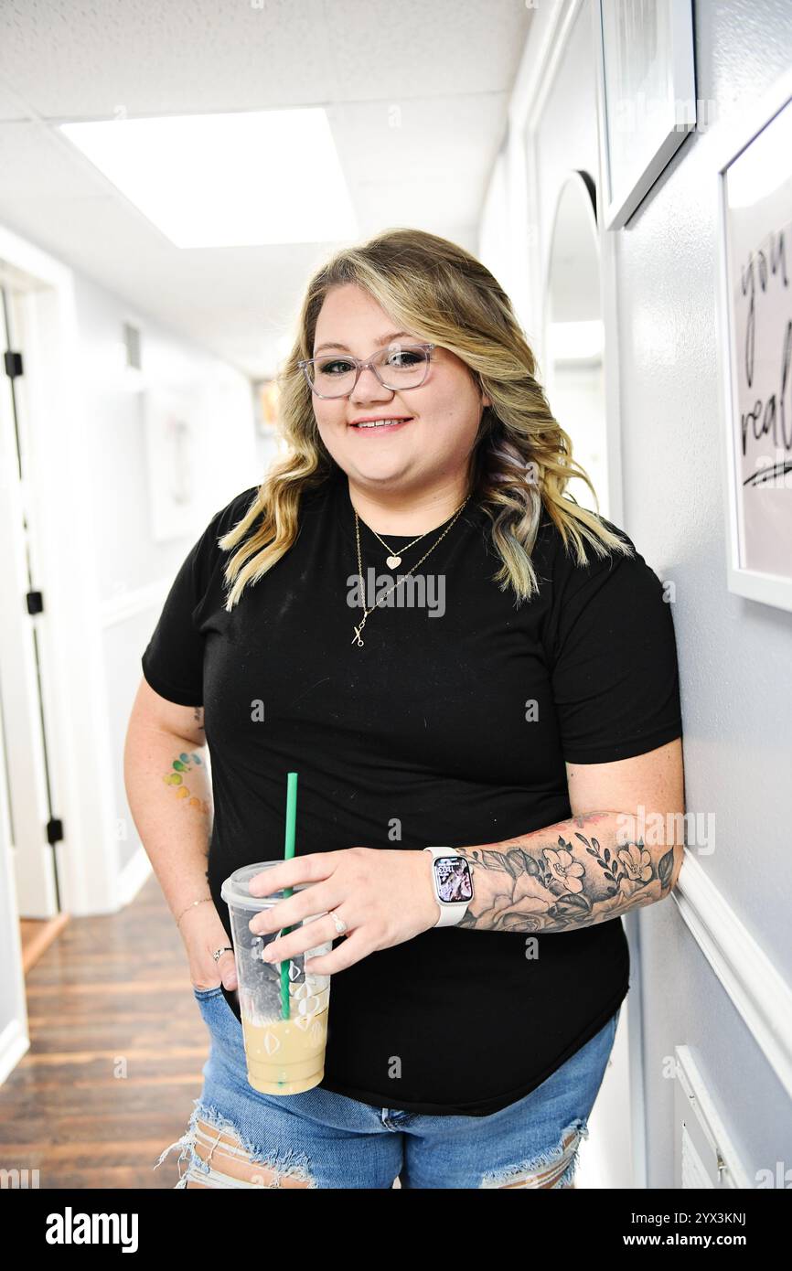 Woman in black shirt, holding iced coffee, smiling in hallway Stock ...