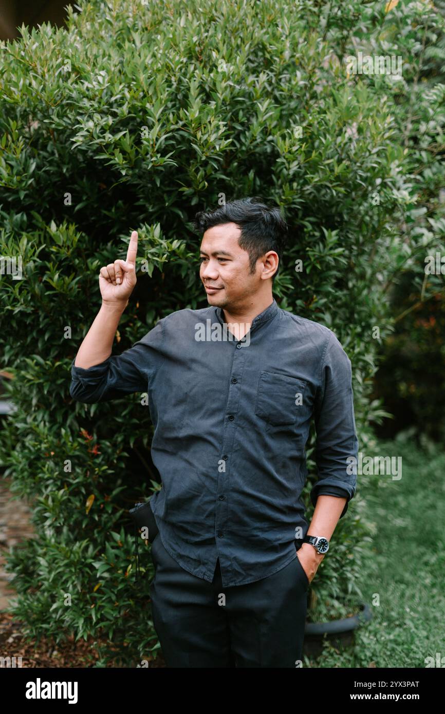 A Southeast Asian man pointing upward with a focused expression ...