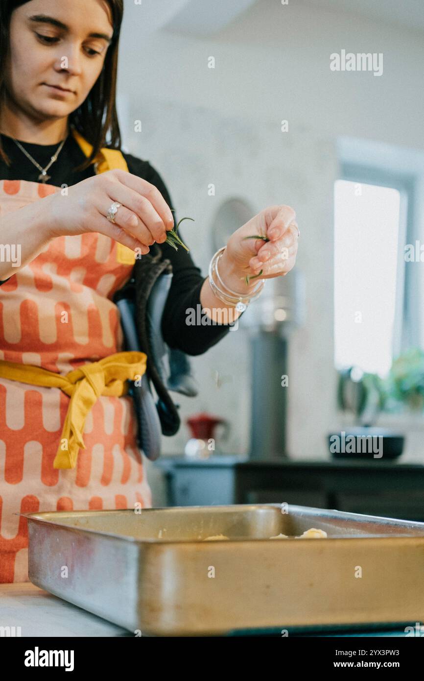 A woman is cooking in a kitchen with a pan on the stove. She is wearing ...