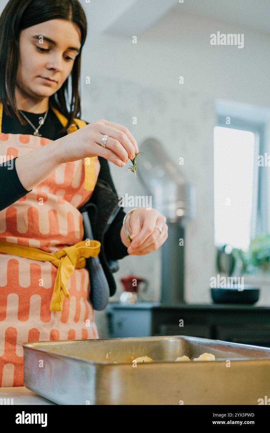 A woman is cooking in a kitchen and sprinkling herbs on a dish. The ...