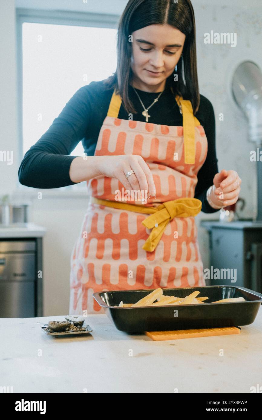A woman is cooking in a kitchen with a black apron and a white apron ...