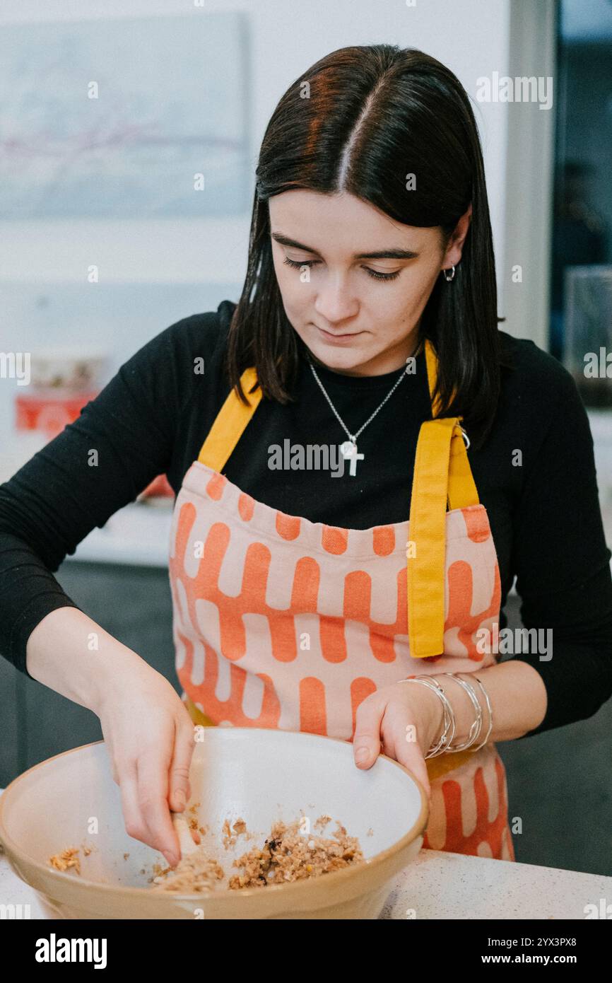 A woman is cooking in a kitchen with a yellow apron on. She is wearing ...
