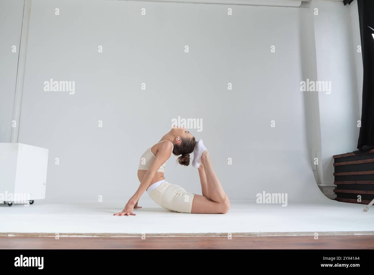 A woman demonstrates an advanced backbend yoga pose in a minimalist ...