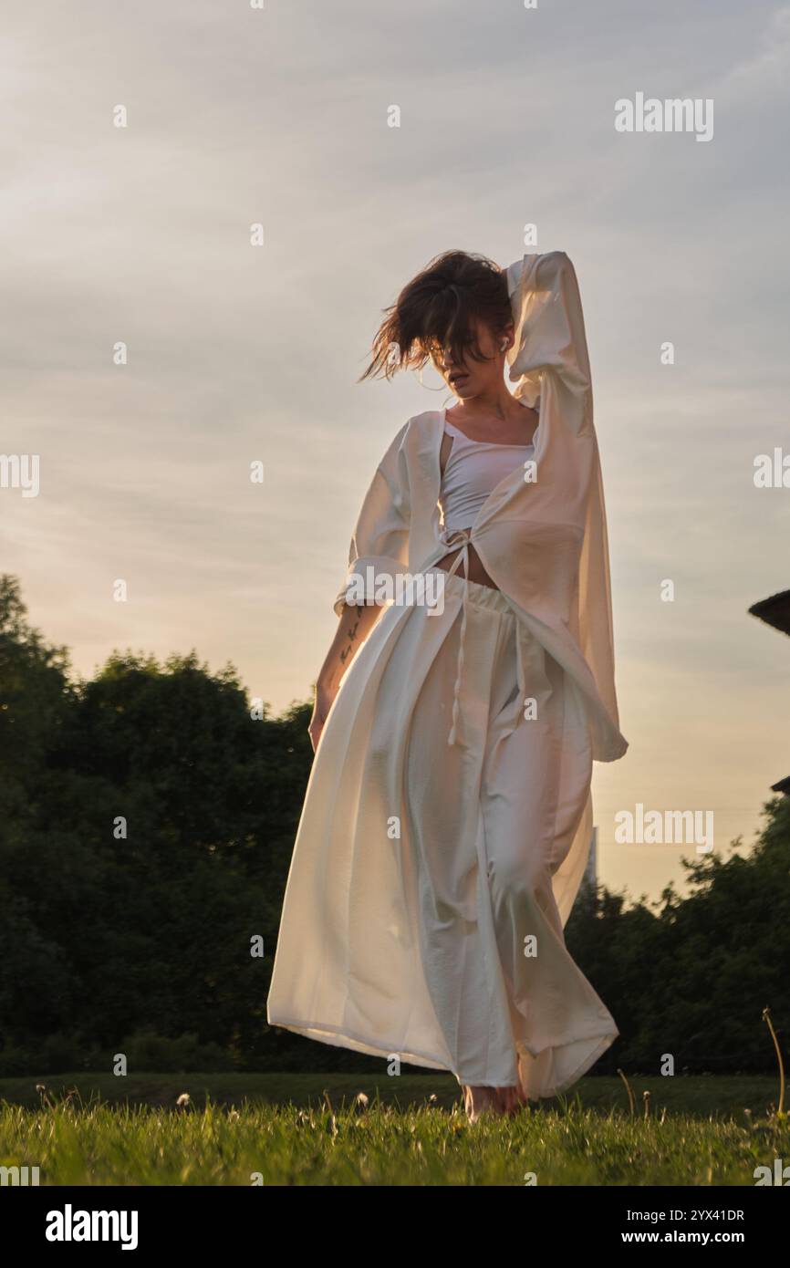 A dancer in a white outfit poses with arms outstretched in a grassy ...
