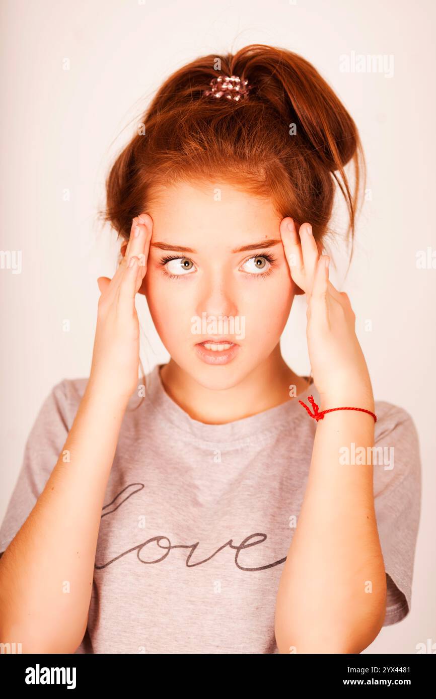 Happy beautiful girl smiling with closed eyes touching her red curly hair over white background ...