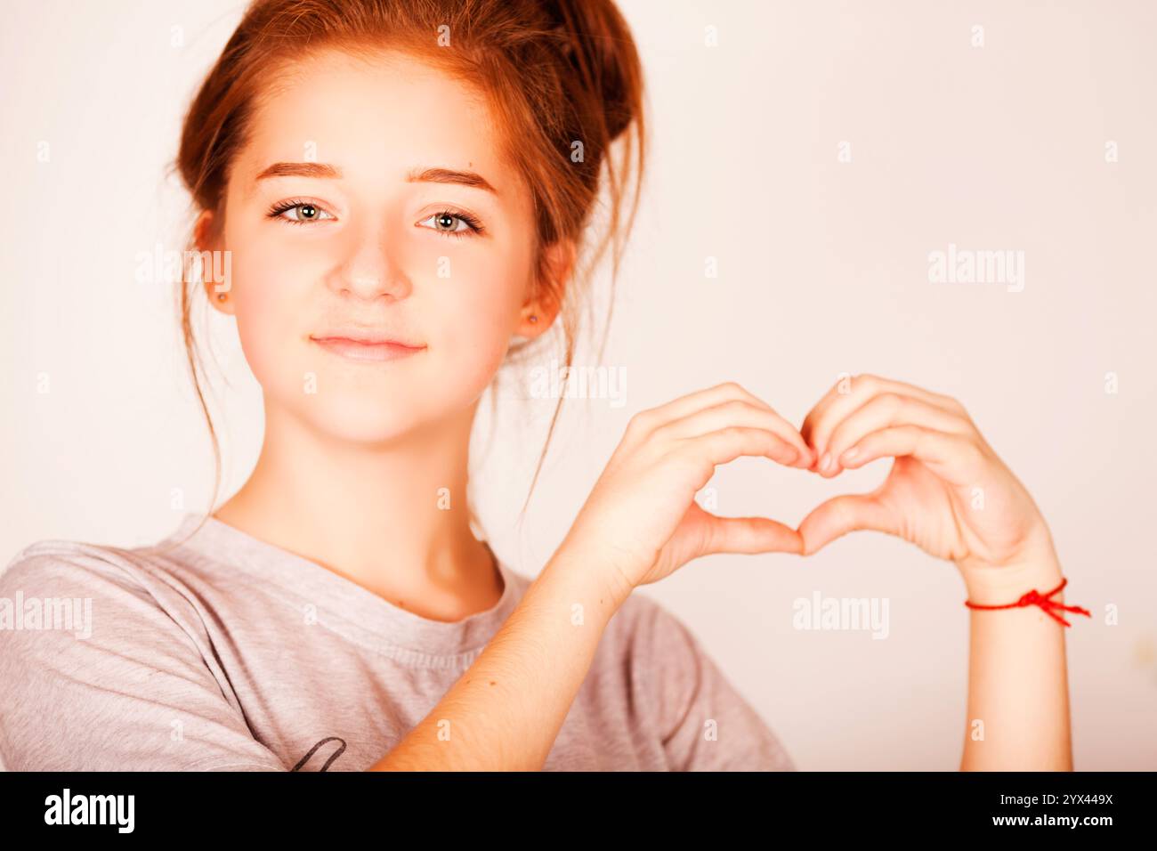 Happy beautiful girl smiling with closed eyes touching her red curly hair over white background ...