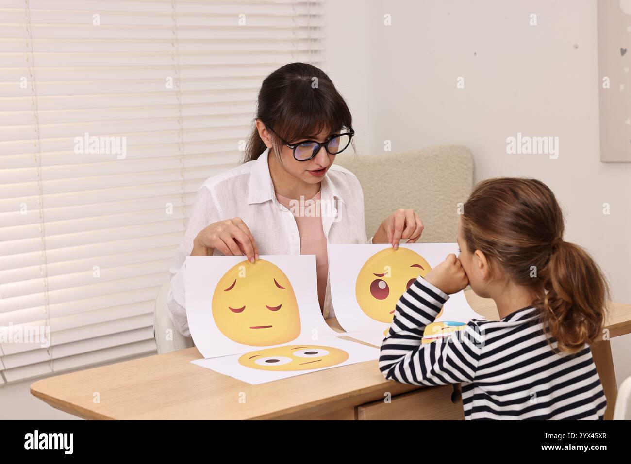 Autism therapy. Little girl choosing emoticon at table with ...